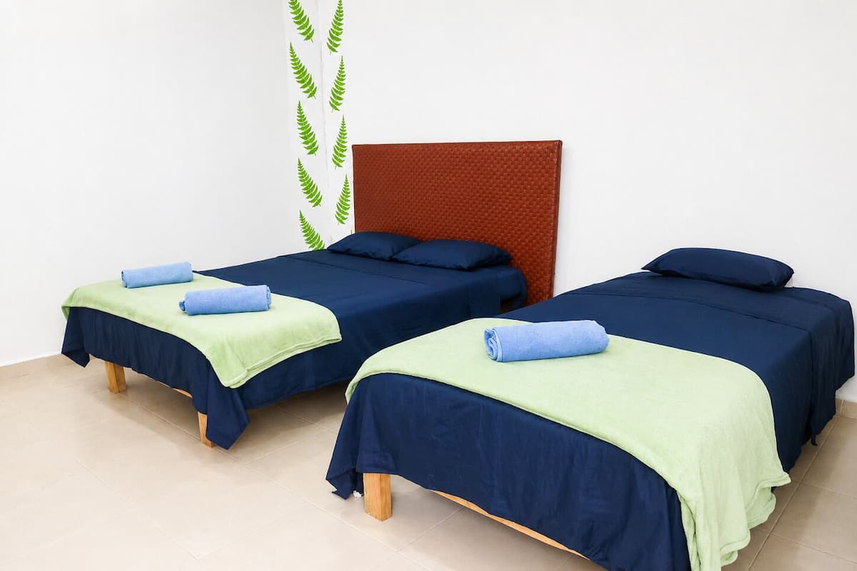 Duas camas de solteiro com roupa de cama azul e verde, pés de madeira e cabeceira vermelha.
