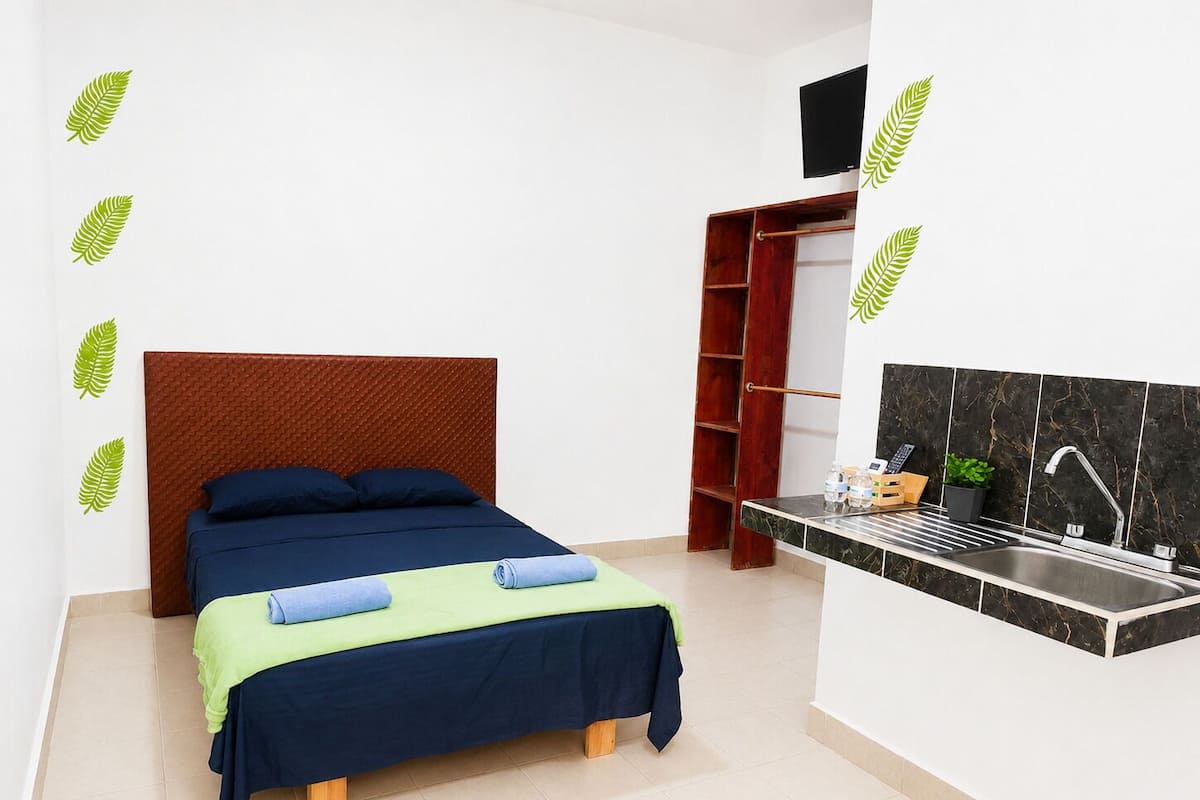 Quarto com cama, cabeceira de madeira, secretária embutida com pia e guarda-roupa.
