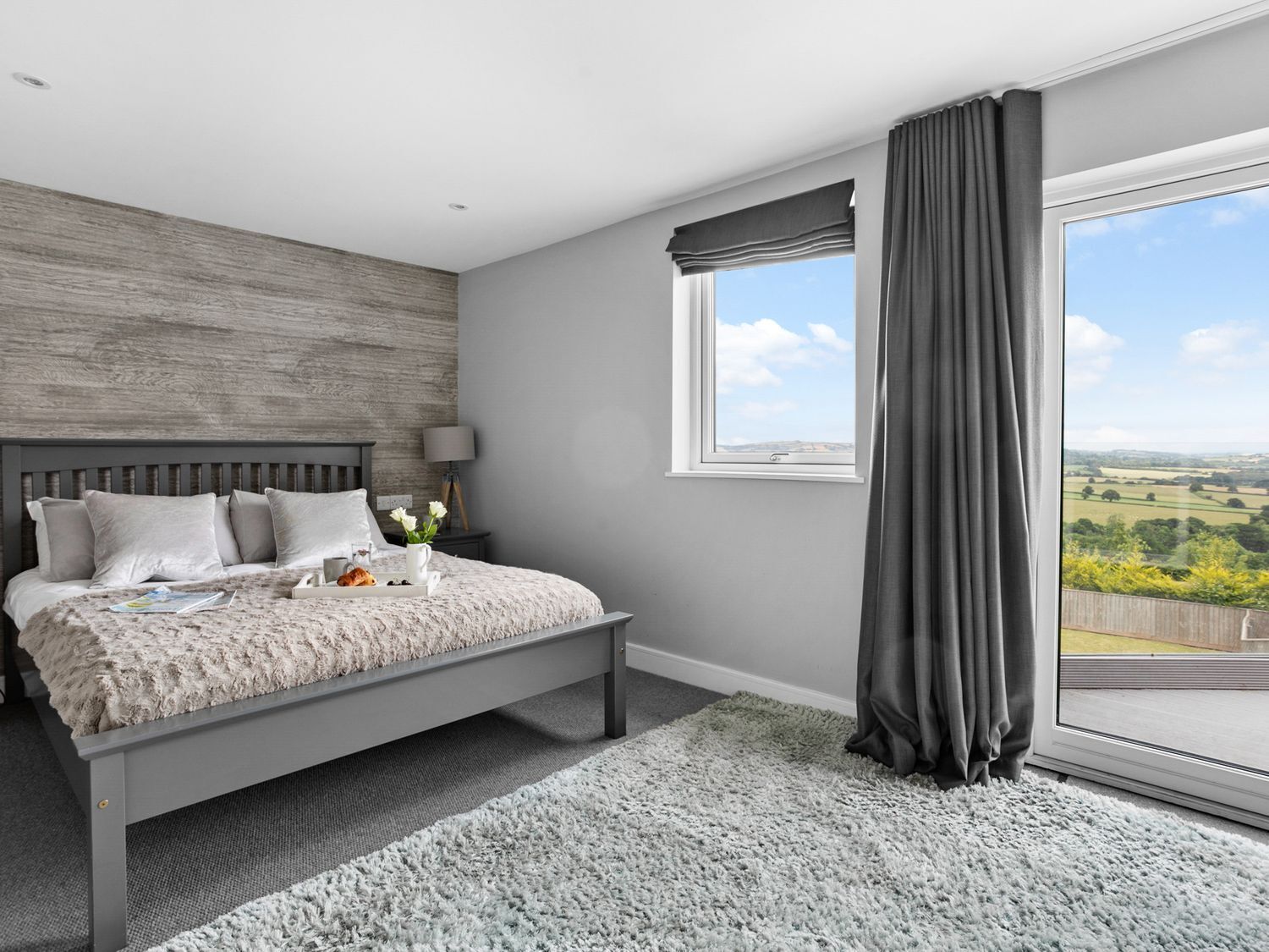 Um quarto moderno com uma cama grande, vista para o campo e janela com cortinas.