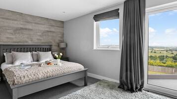 Um quarto moderno com uma cama grande, vista para o campo e janela com cortinas.