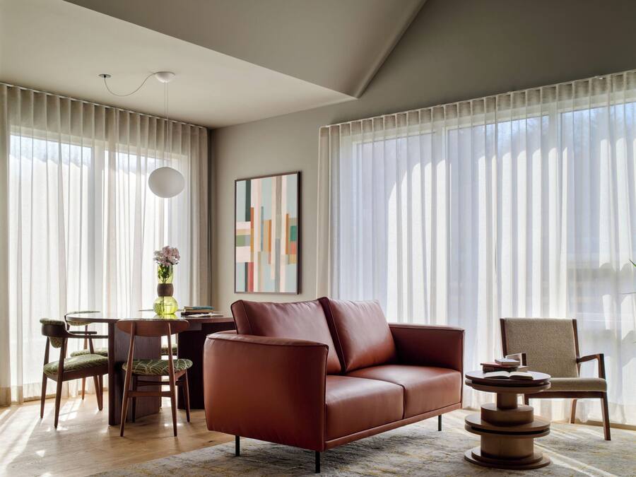 Uma sala de estar moderna com um sofá de couro, uma mesa de jantar com cadeiras e uma janela grande com cortinas leves.