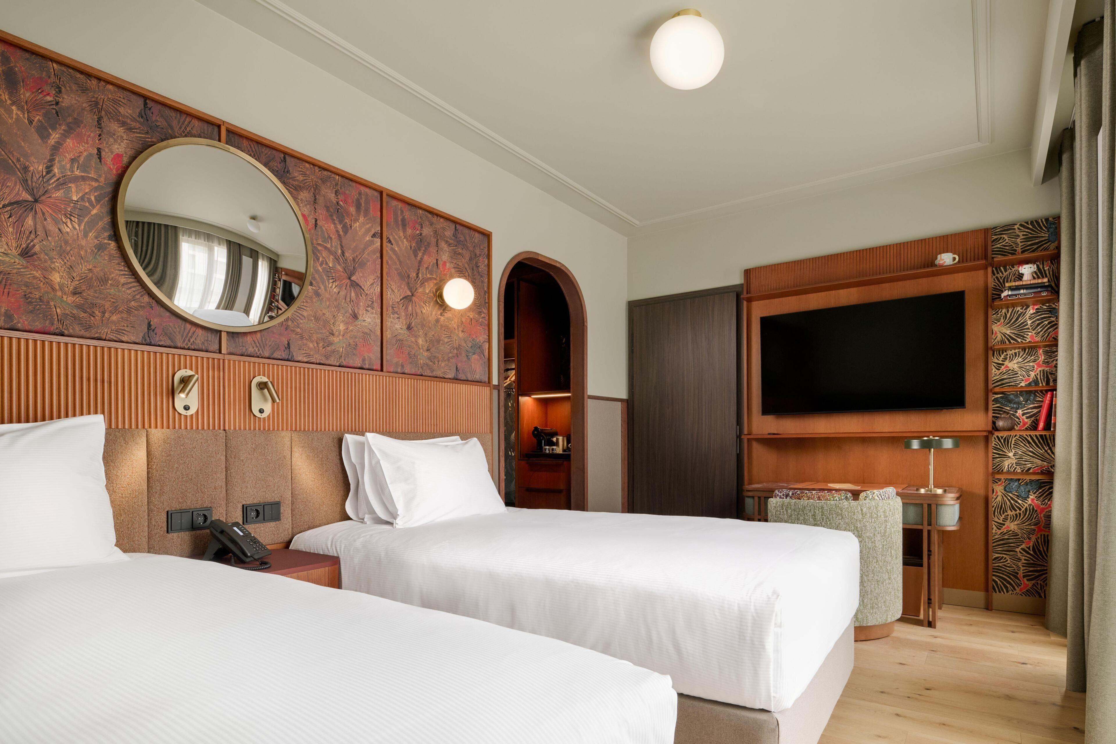 Quarto de hotel com duas camas, um espelho grande, televisão de tela plana e uma estante de livros.