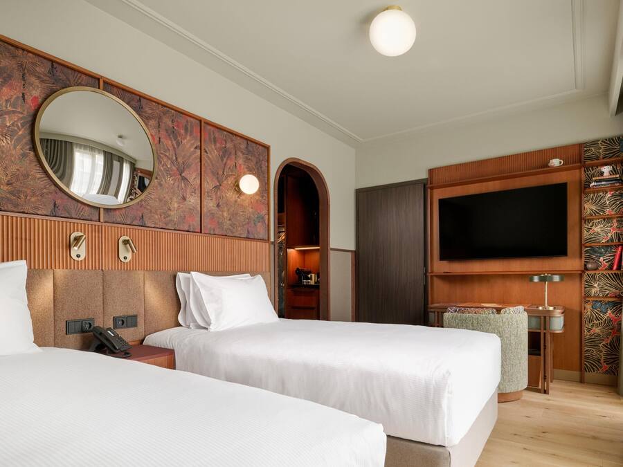 Quarto de hotel com duas camas, um espelho grande, televisão de tela plana e uma estante de livros.