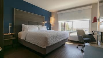 Quarto de hotel com uma cama grande, uma escrivaninha, uma cadeira e uma janela com persianas.