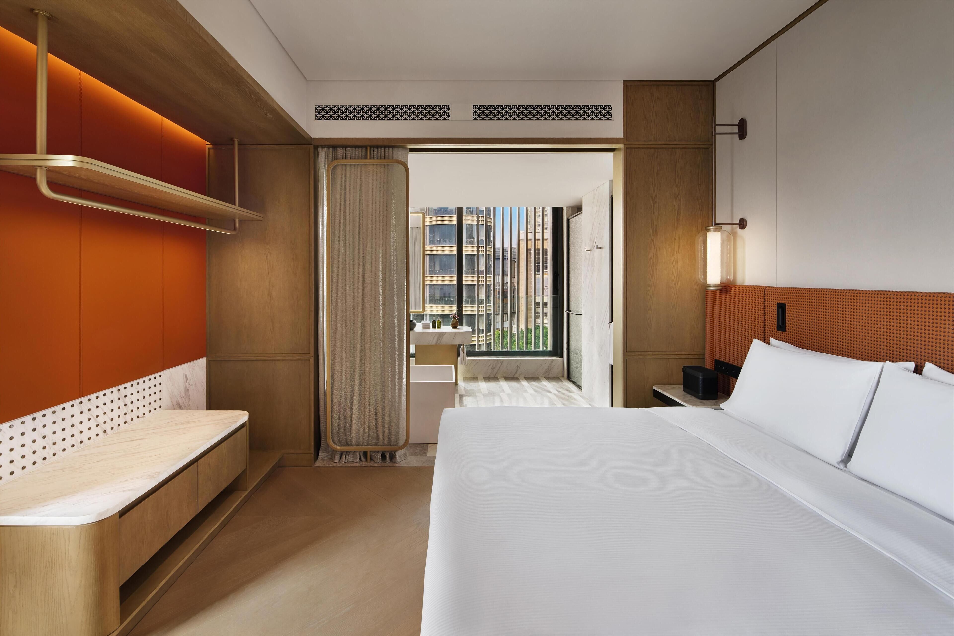 Quarto de hotel com cama, mesa de cabeceira e vista para uma varanda.