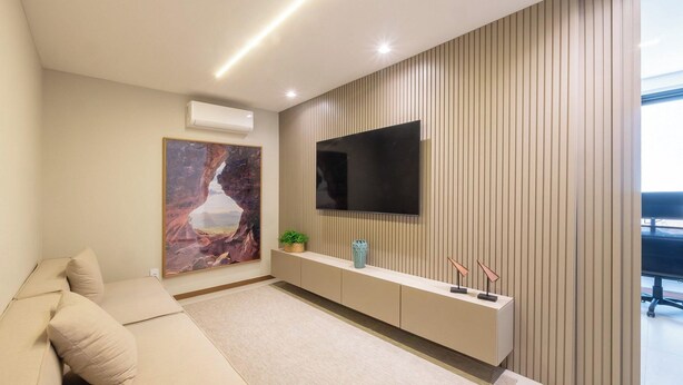 Uma sala de estar moderna com televisão de tela plana presa em parede com lambris, sofá bege e uma grande pintura abstrata.