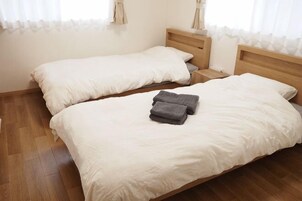 Uma cama de casal com um cobreleito branco e duas almofadas, uma mesa de cabeceira de madeira e um painel de cama de madeira.