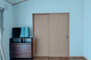 Quarto com guarda-roupa de madeira, televisão sobre um móvel de madeira e parede azul claro.