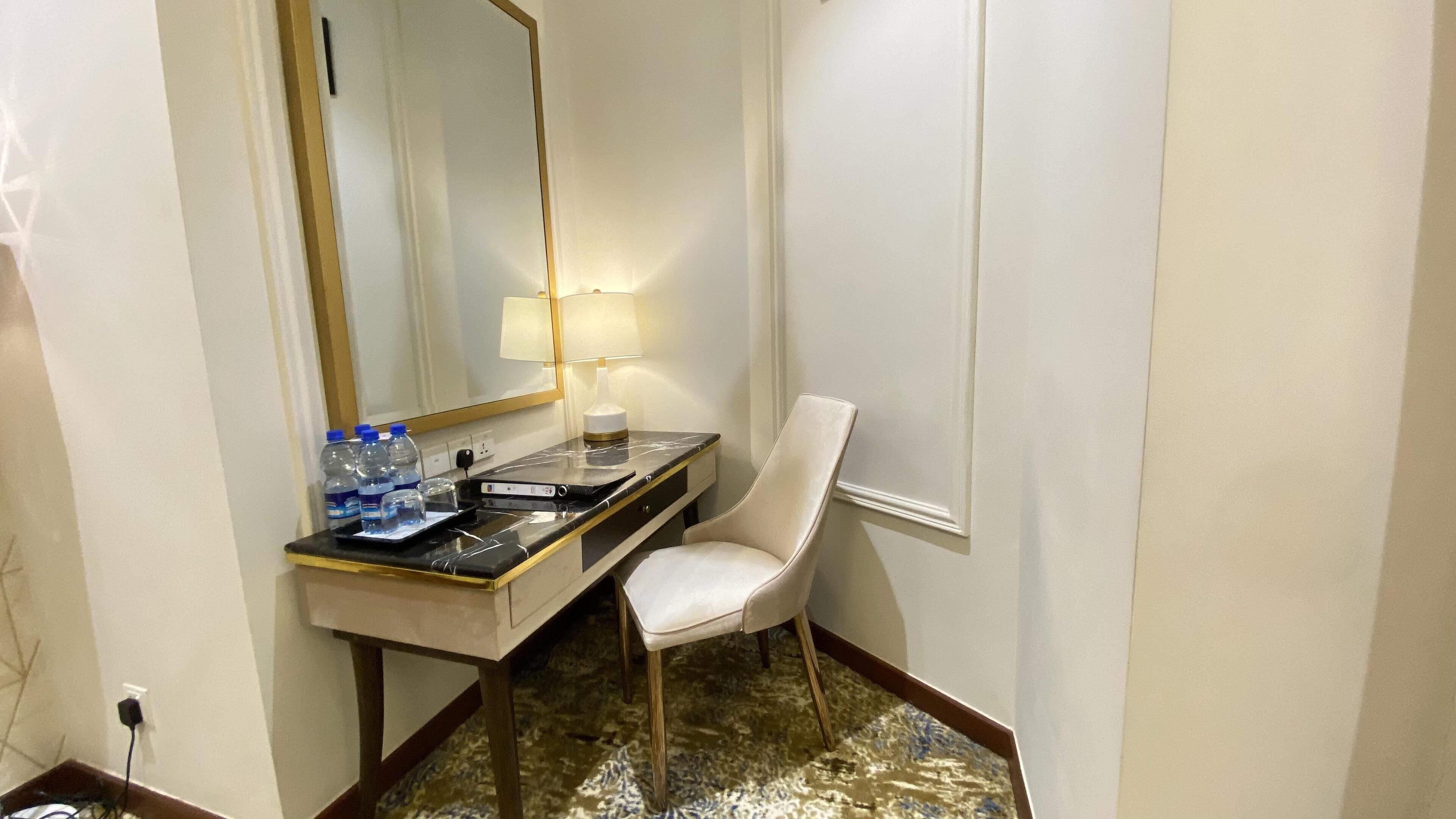 Quarto de hotel com escrivaninha, cadeira e um espelho grande.