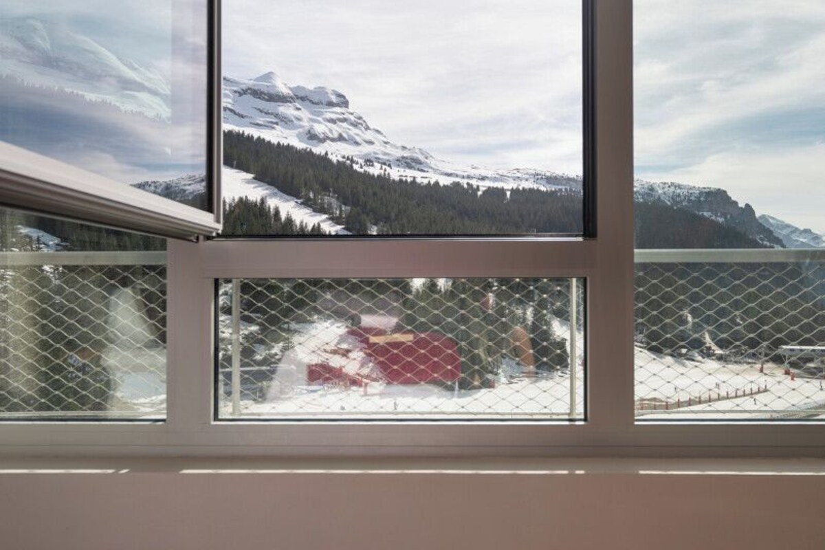 Quarto com uma grande janela com vista para uma paisagem montanhosa coberta de neve.