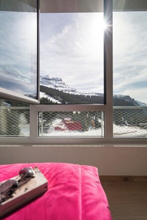 Quarto com uma grande janela com vista para uma paisagem montanhosa coberta de neve.