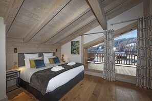 Quarto com uma cama grande, vigas de madeira no teto, vista para uma paisagem nevada e uma varanda com guarda-corpo.