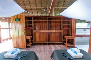 Quarto com paredes de madeira e placa indicando o número 13, prateleiras de madeira e duas mesas de massagem com toalhas e garrafas.