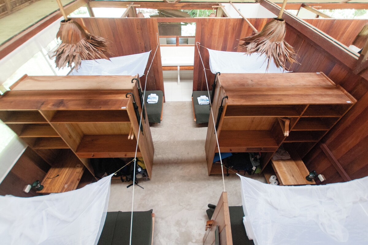 Uma cabana de madeira com quatro beliches, cada um com uma pequena mesa e uma vassoura pendurada.