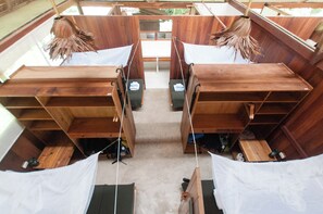Uma cabana de madeira com quatro beliches, cada um com uma pequena mesa e uma vassoura pendurada.
