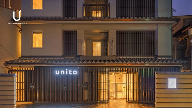 Entrada de hotel com portão, um letreiro com a palavra "unito" e uma varanda sobre a porta.