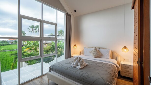 Quarto com uma janela grande, uma cama com manta, duas luminárias de cabeceira e uma mesa de apoio.