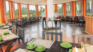 Um restaurante com várias mesas e cadeiras, janelas amplas e vista para o exterior.
