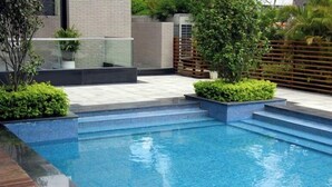 Uma piscina com degraus de acesso, rodeada por um deck de madeira e plantas em vasos.