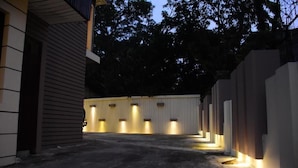 Um edifício moderno com vários janelões iluminados e um caminho de concreto que leva a um portão.