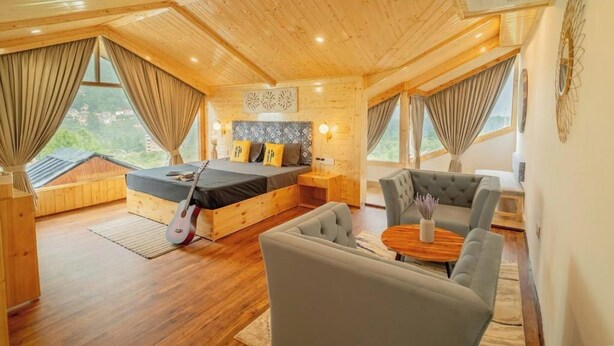 Um quarto aconchegante com uma cama, um violão e um espaço de estar com mesa e cadeiras.