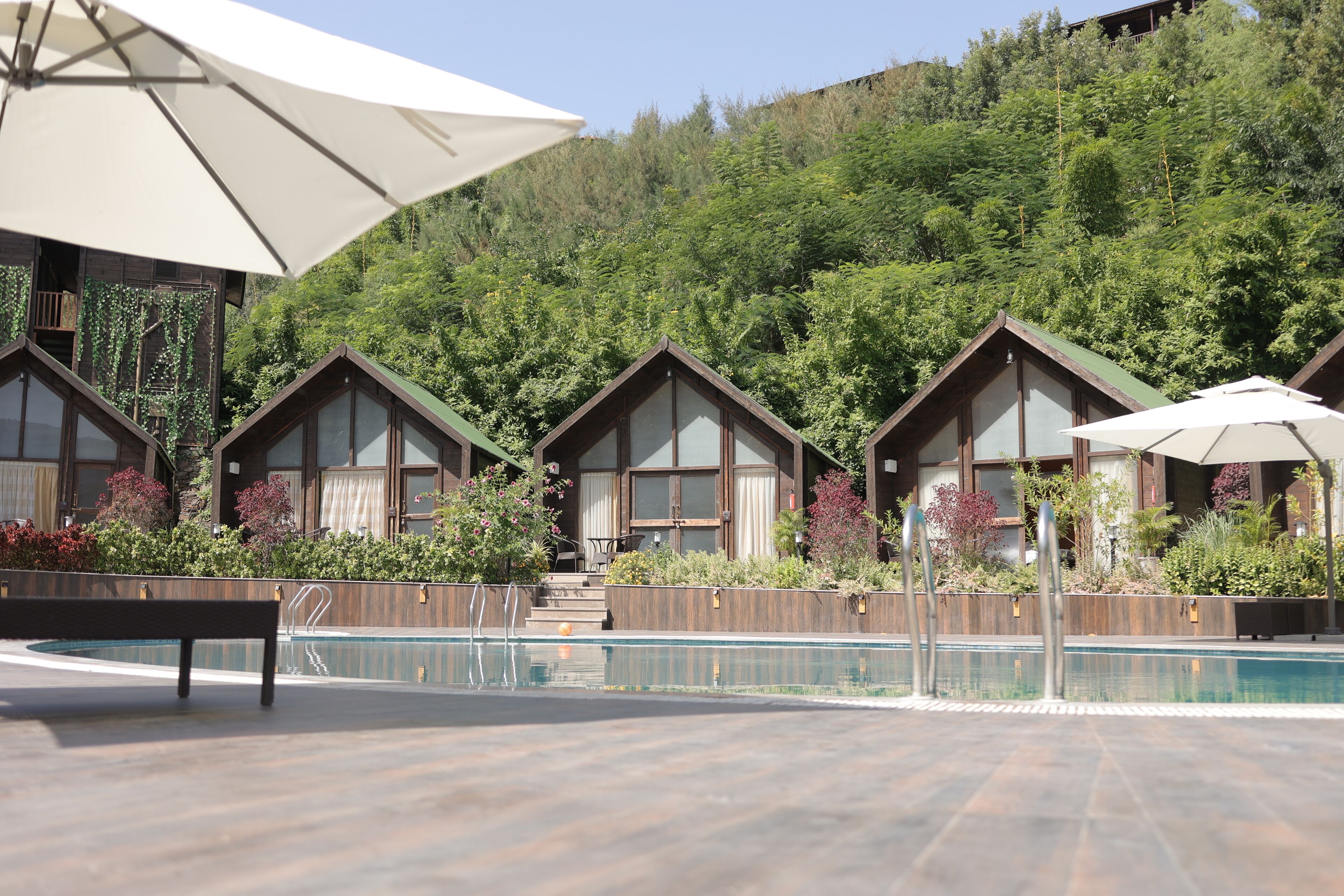 Uma área de piscina com cabanas de madeira, um banco e guarda-sóis.
