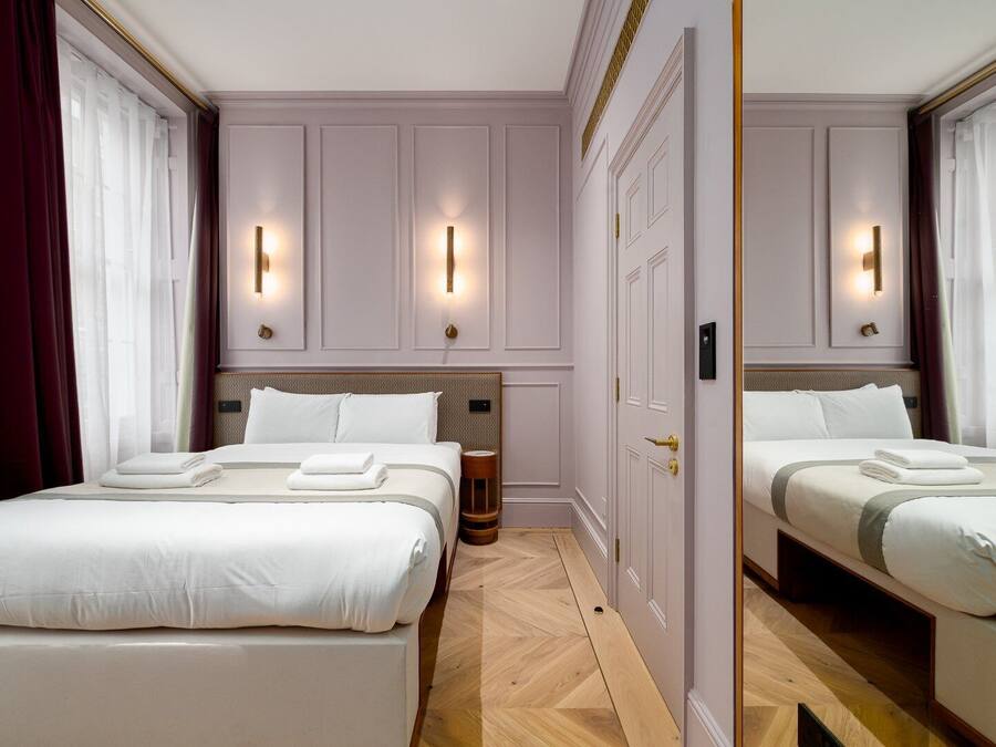 Quarto de hotel com duas camas, piso de madeira e um espelho refletindo o ambiente.