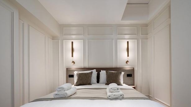 Quarto de hotel com uma cama grande, cabeceira com iluminação embutida e luminária fixada na parede.