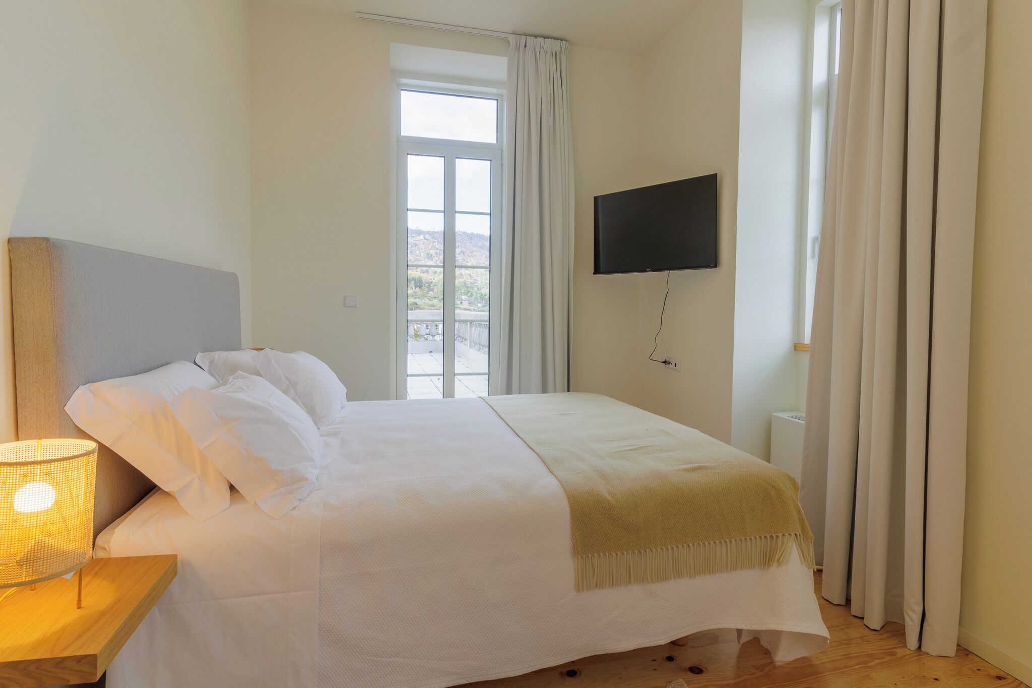 Quarto com uma cama, televisão na parede e janela com cortinas.