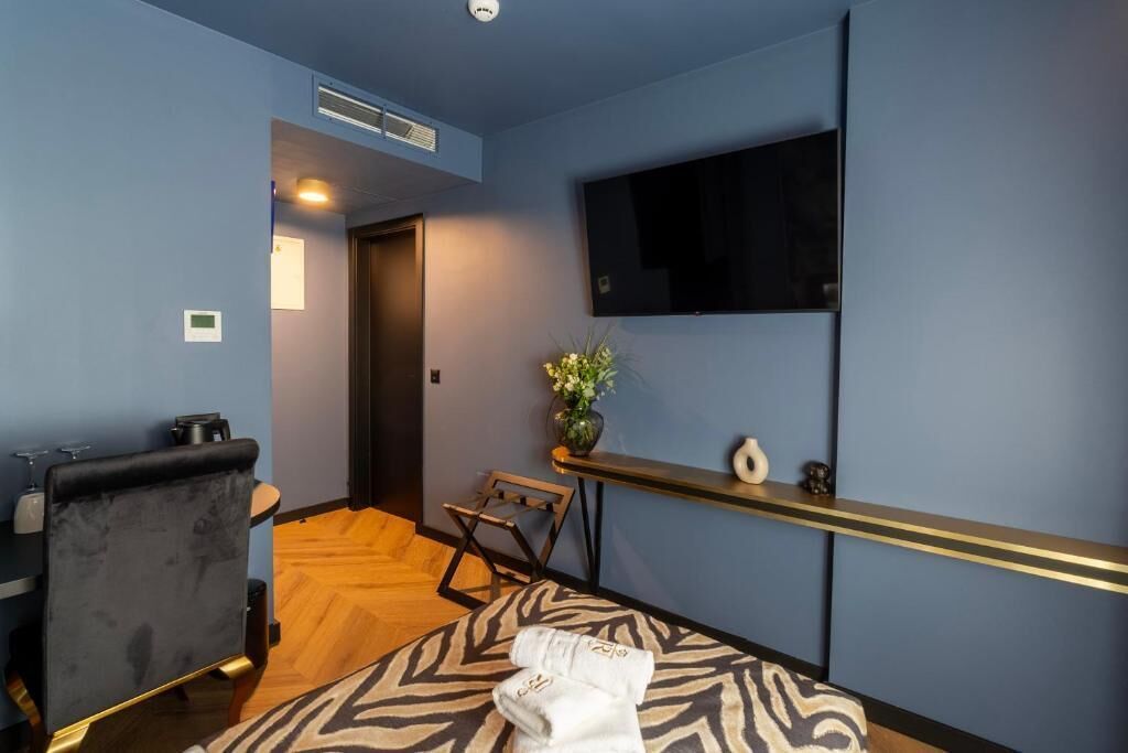 Quarto com cama, escrivaninha, cadeira, televisão e uma pequena mesa com um vaso.