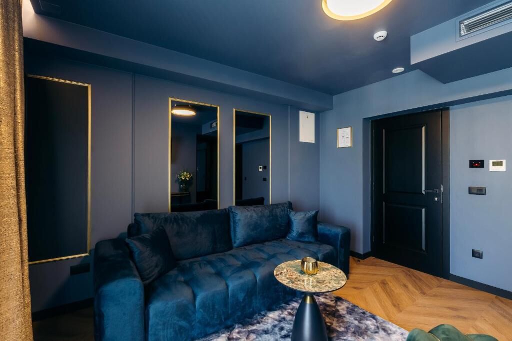 Uma sala de estar moderna com um sofá azul escuro, uma mesa de centro redonda e um espelho com moldura dourada.