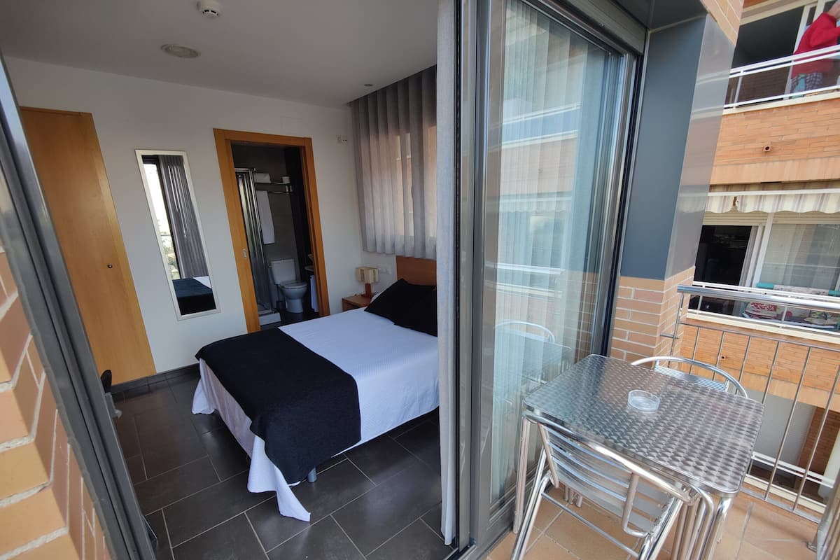Quarto de hotel com cama, banheiro, varanda com mesa e cadeiras, e vista para o exterior.