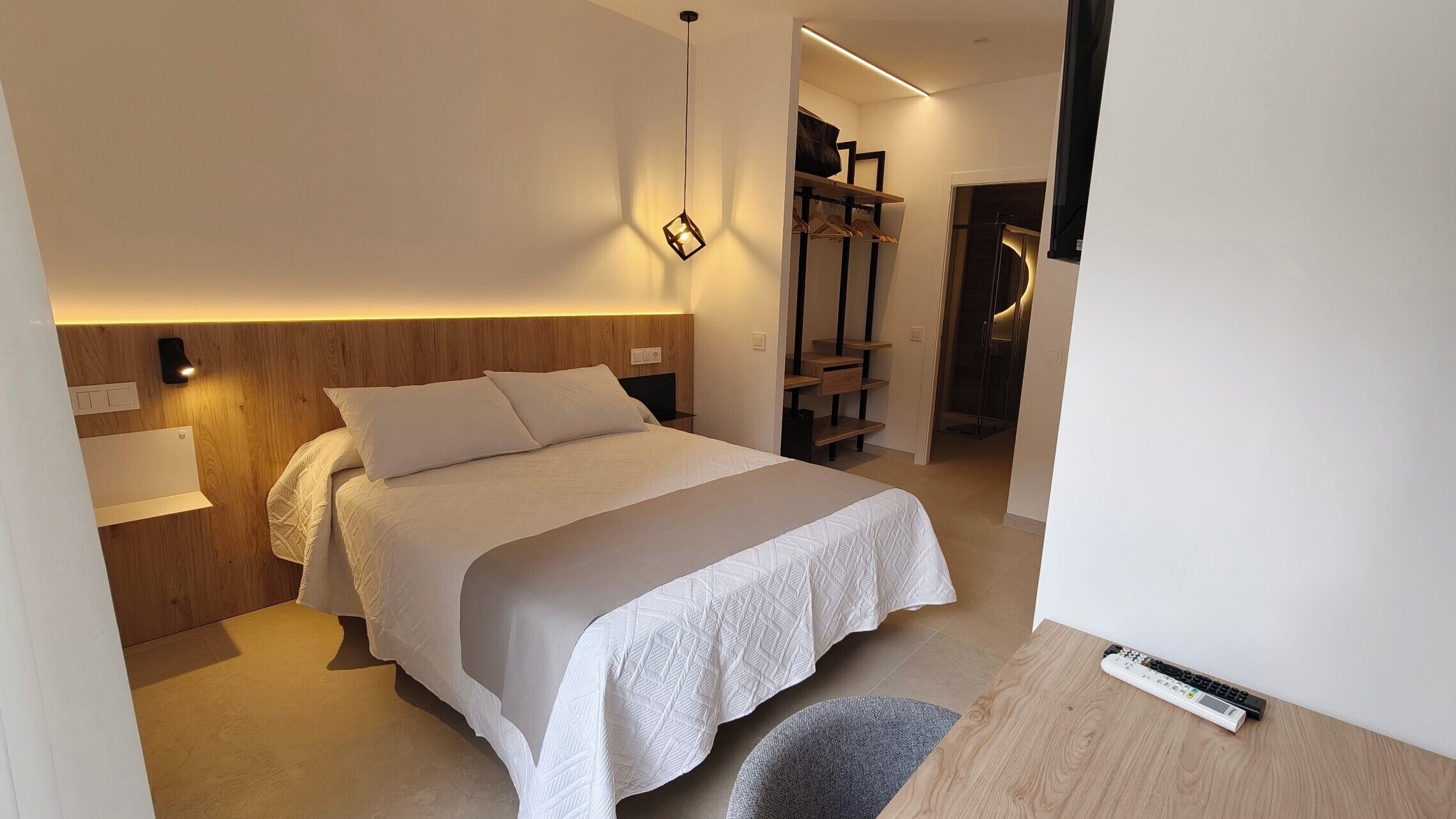 Quarto de hotel moderno com cama bem arrumada, mesa de cabeceira, luminária na parede e guarda-roupa embutido.