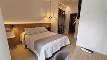 Quarto de hotel moderno com cama bem arrumada, mesa de cabeceira, luminária na parede e guarda-roupa embutido.