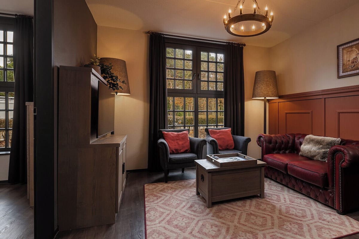 Um quarto com lareira, duas poltronas, um sofá, uma mesa de centro e um candelabro.