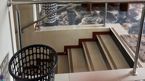 Corredor de hotel com corrimão de metal, um cesto de lixo e piso estampado.