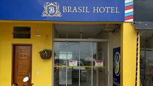 Entrada de hotel com fachada azul e amarela, uma motocicleta estacionada na frente e uma placa indicando área de estacionamento.