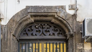 Um portão de metal preto com um arco decorativo, embutido em uma parede de pedra com uma placa de identificação.