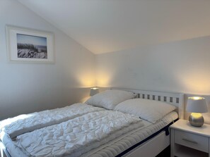 Quarto com cama, duas luminárias de cabeceira, uma mesinha de cabeceira e um quadro na parede.