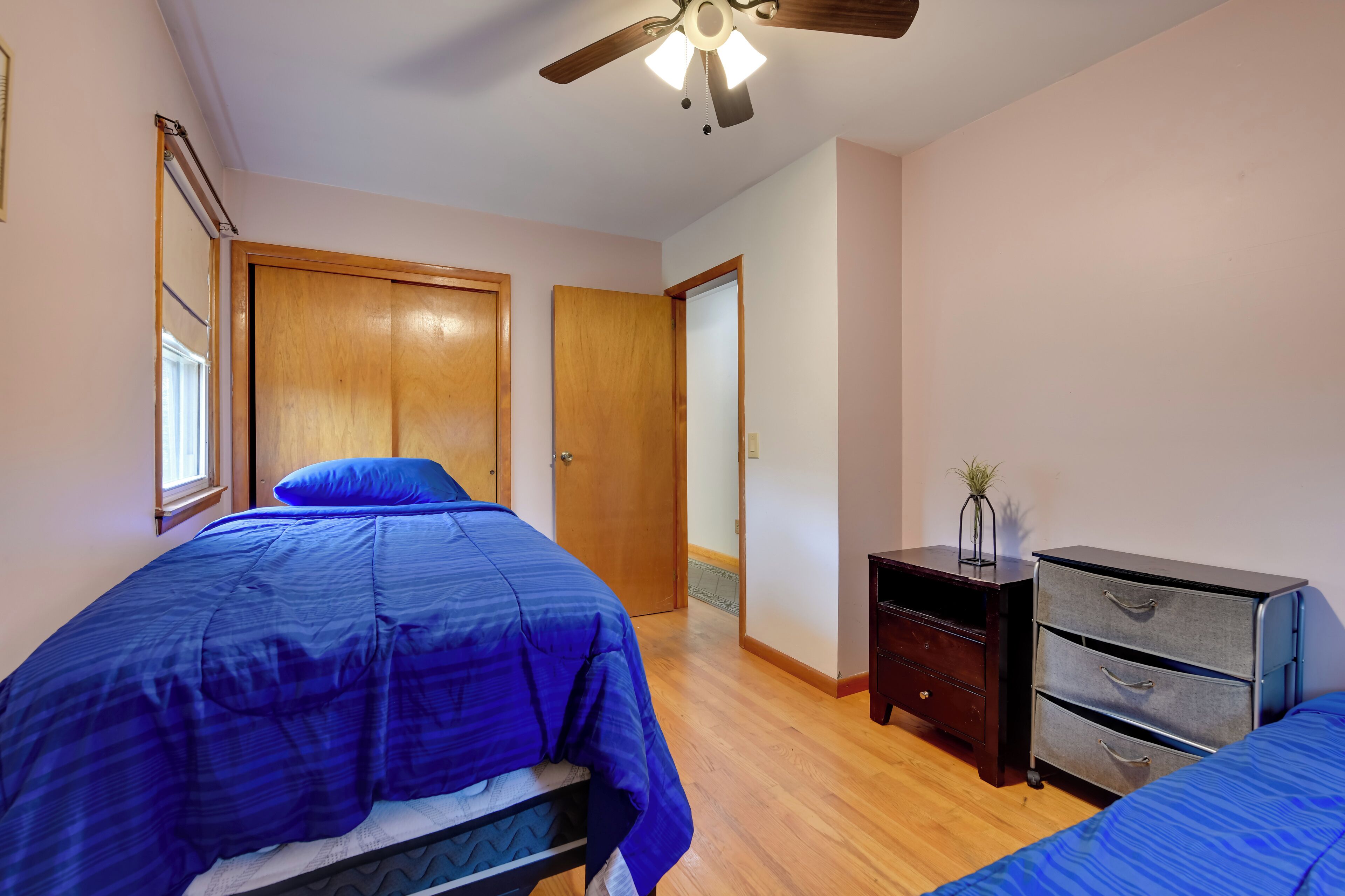 Quarto com duas camas, portas de madeira, cômoda e ventilador de teto.