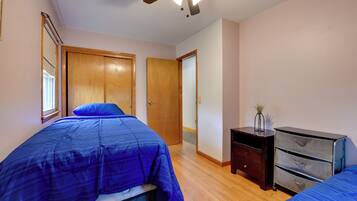 Quarto com duas camas, portas de madeira, cômoda e ventilador de teto.