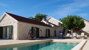 Um edifício de pedra com piscina, área de estar ao ar livre e cadeira suspensa.