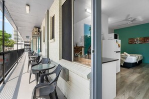 Uma varanda com área de estar ao ar livre, cozinha com geladeira e quarto com cama e ventilador de teto.