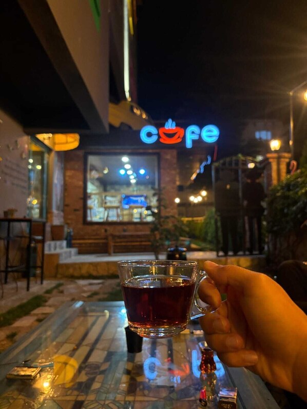 Uma chávena de chá sobre uma mesa, em frente a um café à noite.