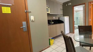 Cozinha compacta equipada com micro-ondas, geladeira e área de refeições com mesa de vidro e cadeiras de vime.