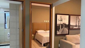 Quarto de hotel com cama, uma cadeira e duas fotografias emolduradas na parede.