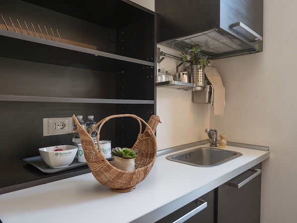 Cozinha moderna com bancada branca, pia de aço inoxidável e cesto de vime com uma pequena planta pendurada.