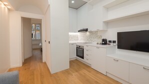 Uma cozinha moderna com armários brancos, forno embutido e uma grande televisão de tela plana.