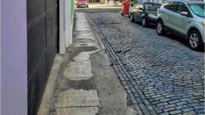 Uma rua de paralelepípedos estreita, ladeada por edifícios, incluindo um prédio de esquina amarelo e um prédio azul com detalhes brancos.