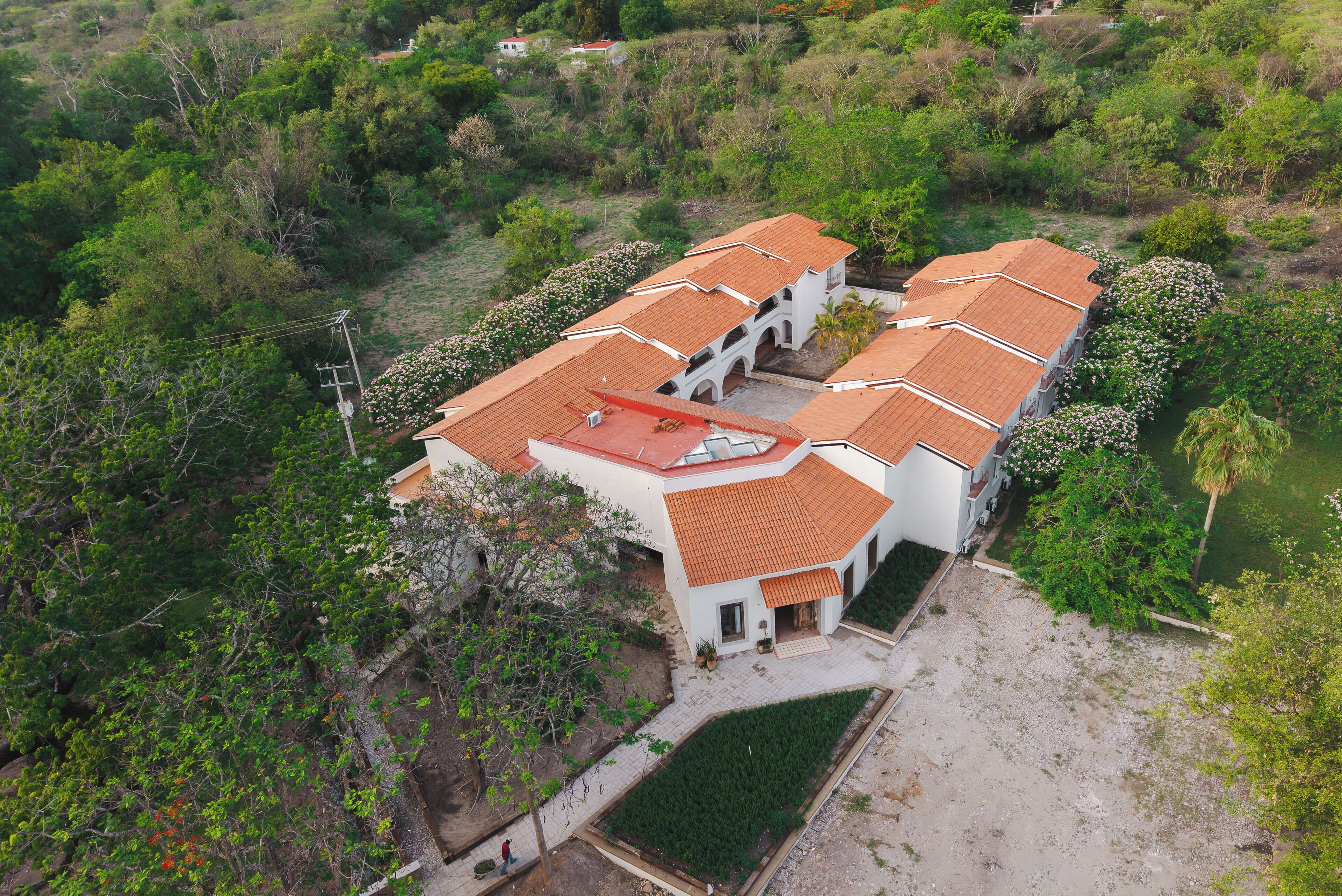 Vista aérea de um edifício branco com telhado de telhas vermelhas, rodeado por vegetação.